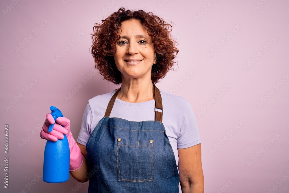 Middle age curly hair woman cleaning doing housework wearing apron and ...