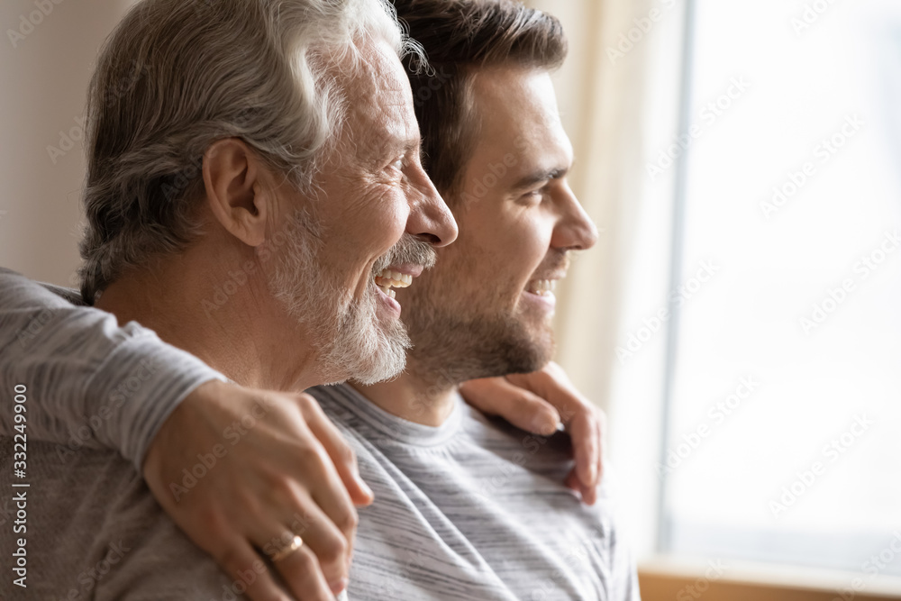 Close up of elderly father and adult grown-up son hug look in distance ...