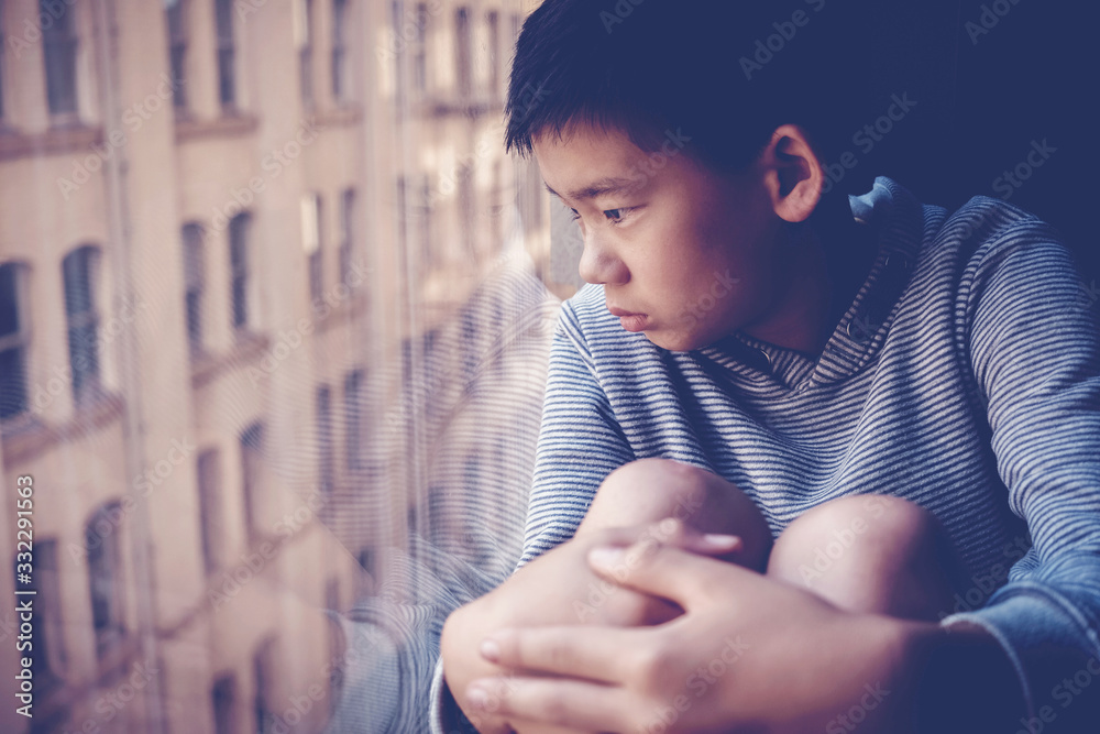Sad Asian preteen boy feeling lonely, looking out of window from his ...