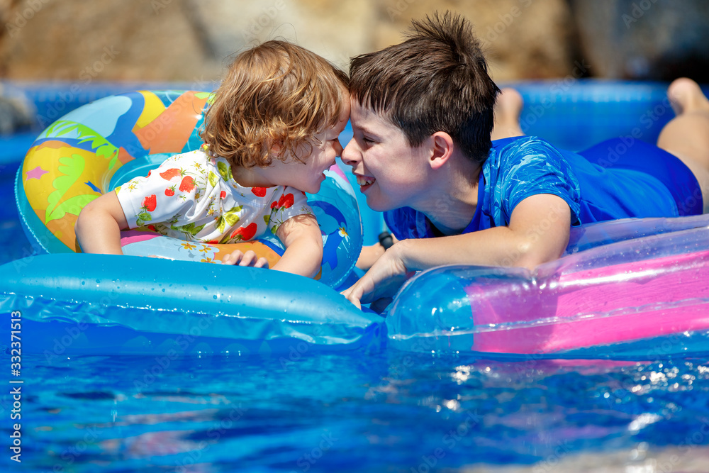 Kids playing in swimming pool. Big brother together with his little ...