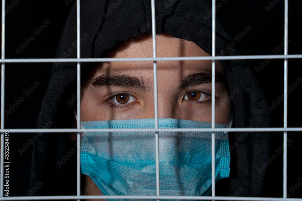 a teenager with thick black eyebrows in a black hood and a disposable ...