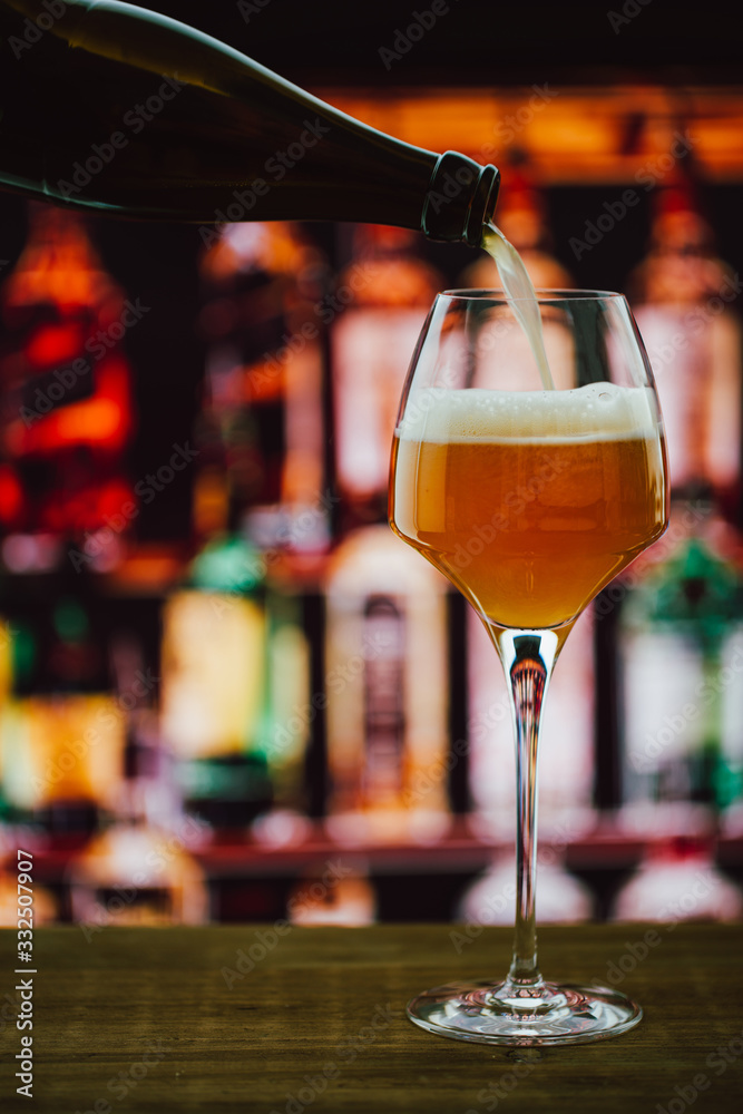 Beer in wineglass with foam in glass on wooden counter in bar on blur ...