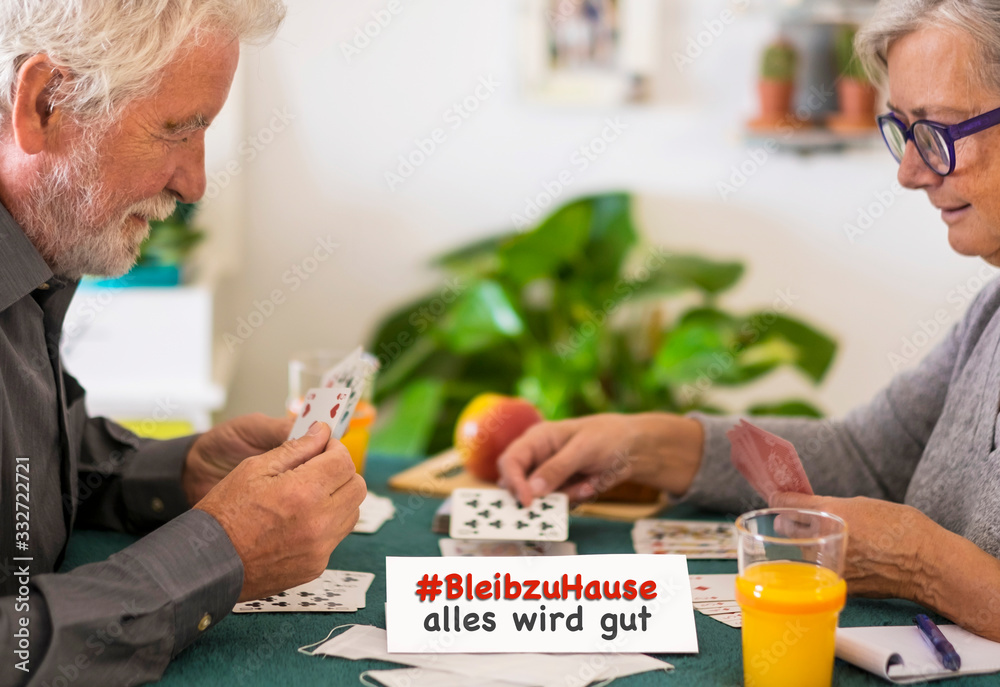 German text saying "stay home, everything will be fine". Two elderly people playing cards at ...