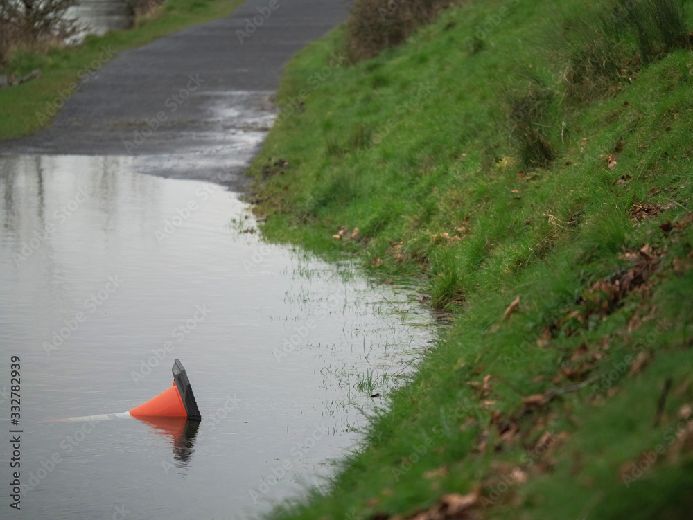 Traffic cone in water during flood by a river. Part of a foot path ...