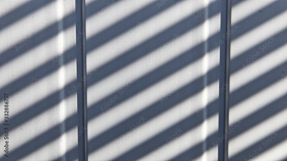 Vertical white plastic planks with grey diagonal sun rays shadows close ...
