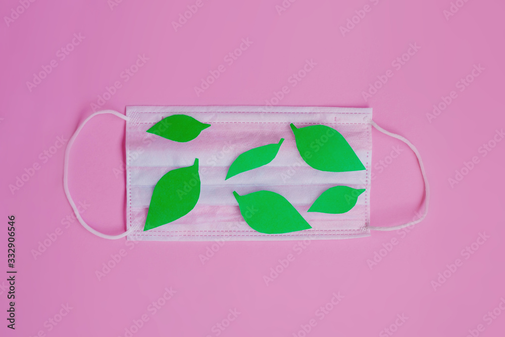 Medical mask, green paper leaves on a pink background. Virus and spring ...