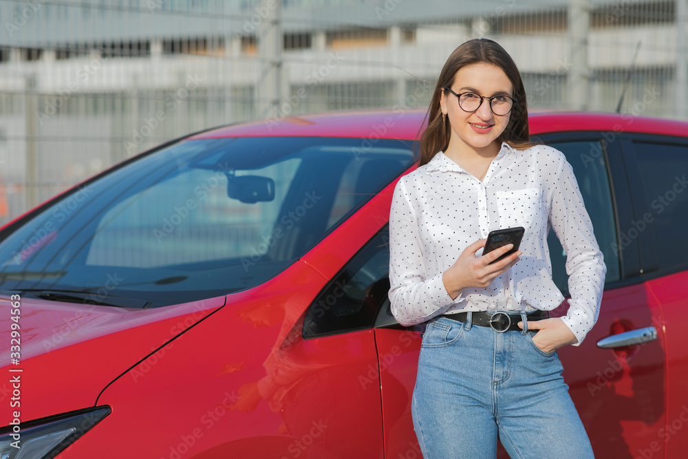 Girl stands with phone near her red electric car and waits when vehicle ...