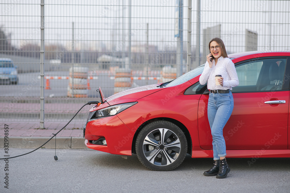 Ecological Car Connected and Charging Batteries. Girl Use Coffee Drink While Using SmartPhone ...