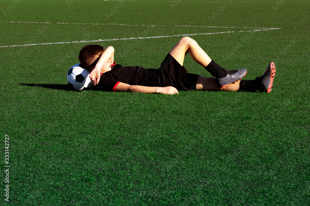 Cute boy soccer player lies on the grass of a football field, resting ...