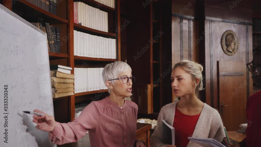 Focused university students talking with teacher in library. College ...