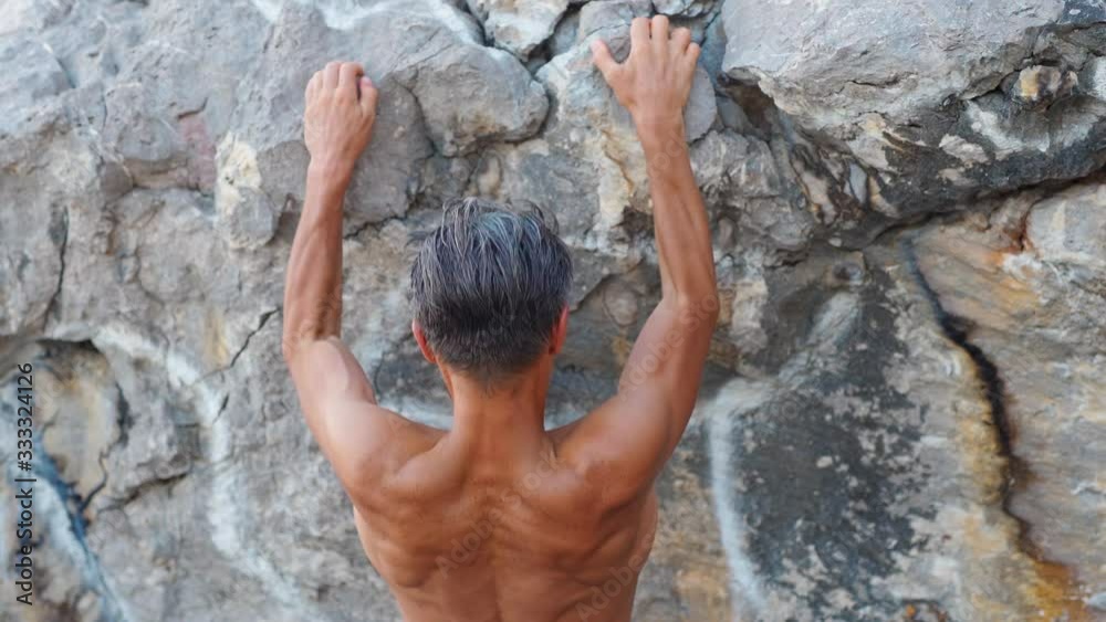back view athletic tanned man rock climber doing pull ups on limestone ...