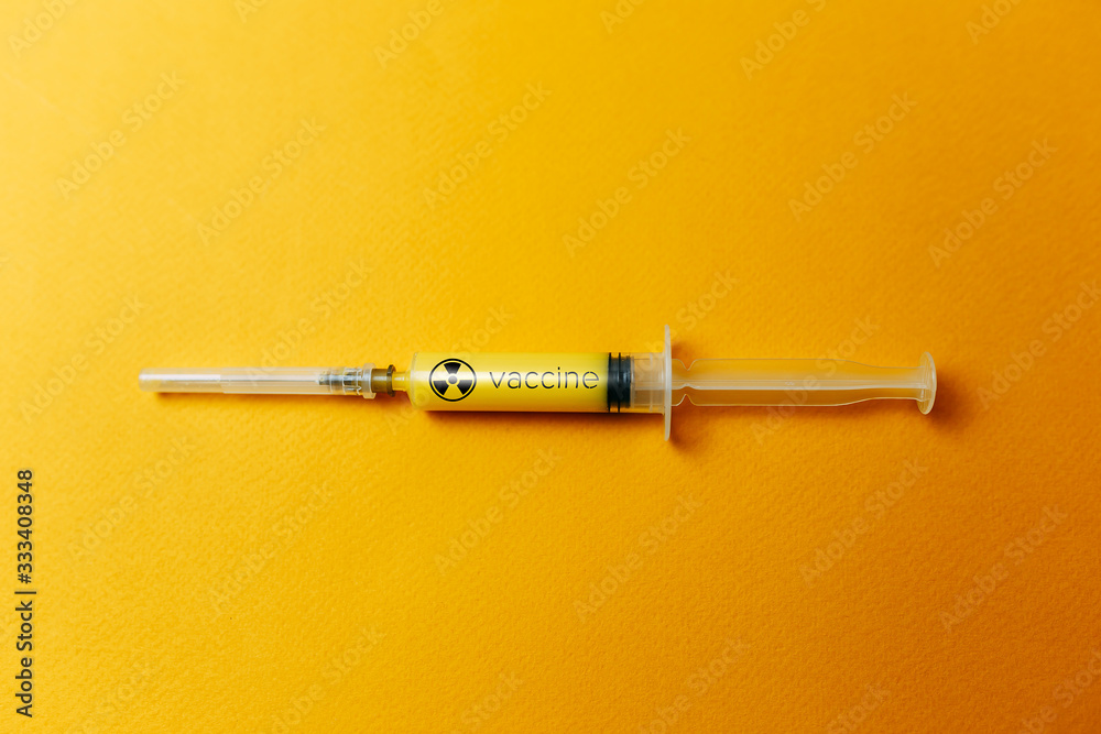 Yellow syringe with biohazard sign on orange background. Coronavirus vaccine in white medicine ...
