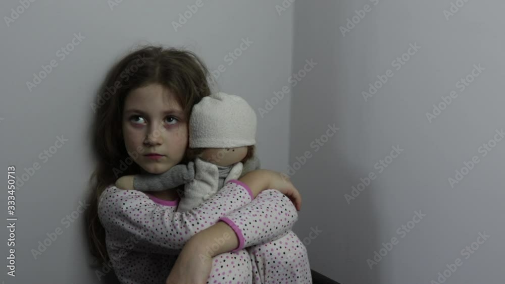 little girl with a doll is sitting in the corner and crying. the ...