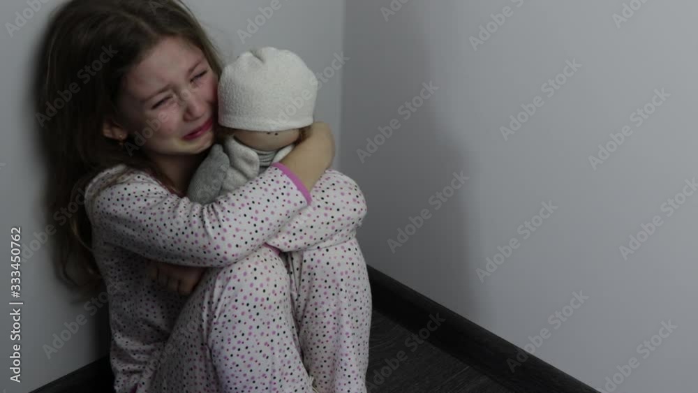 little girl with a doll is sitting in the corner and crying. the ...
