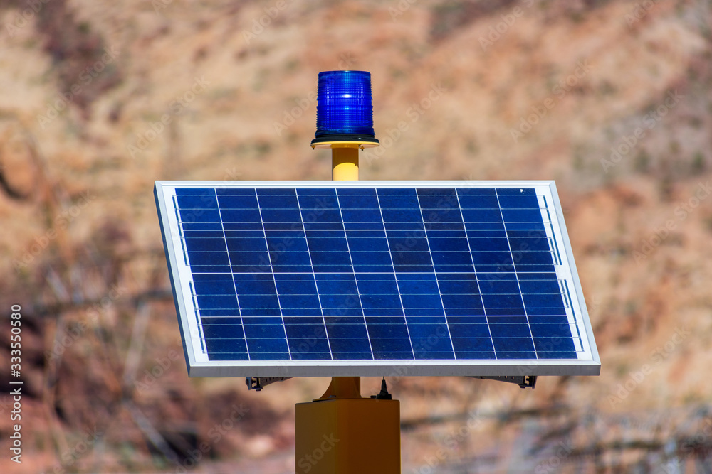 Blue emergency light fixture powered by solar panel. Blurred desert ...