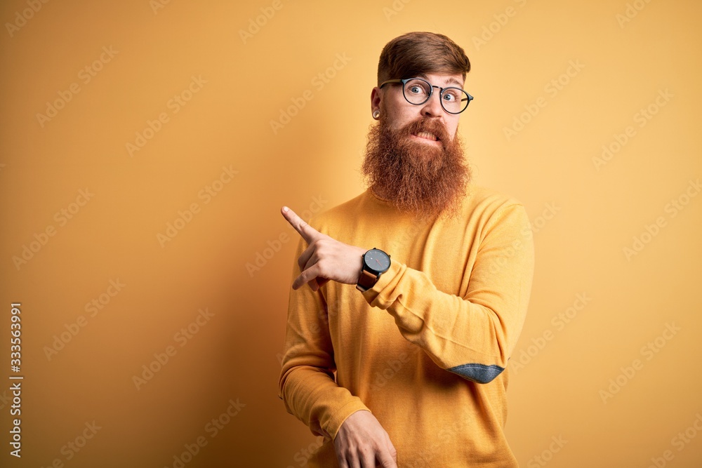 Handsome Irish redhead man with beard wearing glasses over yellow ...