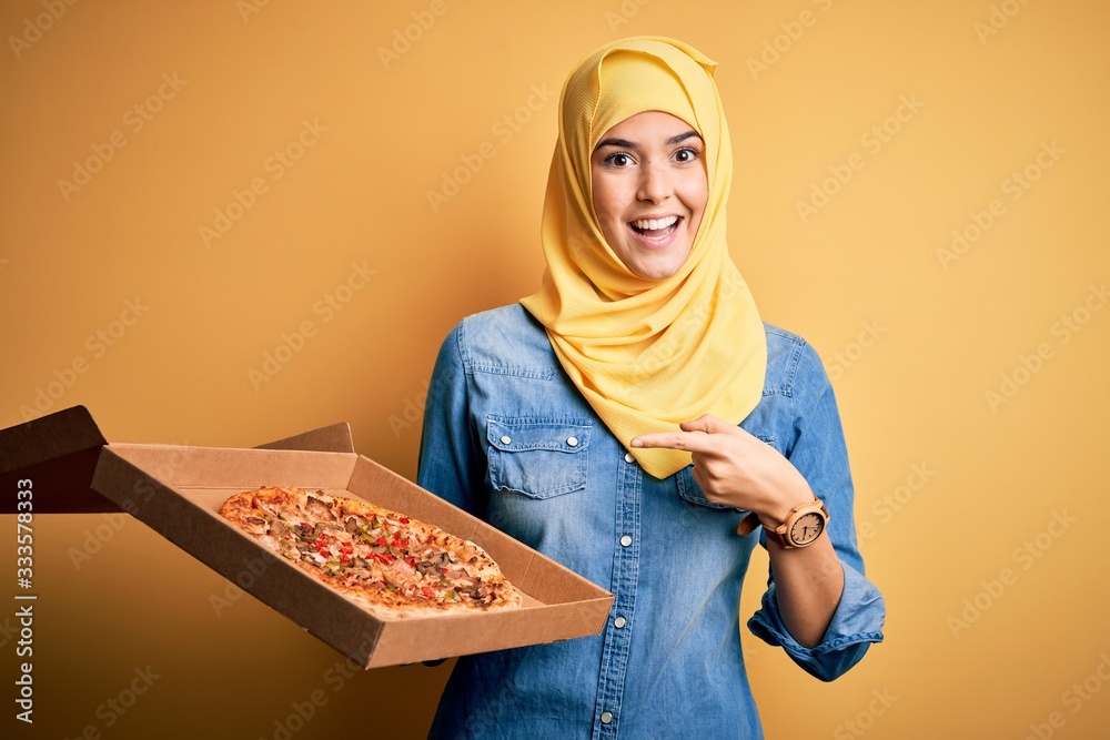 Young girl wearing muslim hijab holding box with Italian pizza over ...