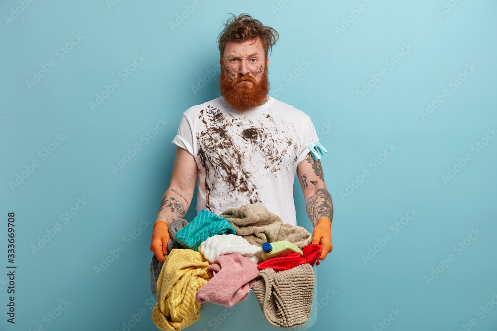 Foto de Displeased dirty man with ginger beard stands with basin full ...