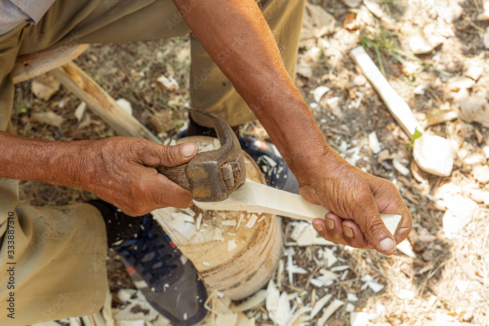 Old man handcrafting a wood sppon the traditional way of making tools ...