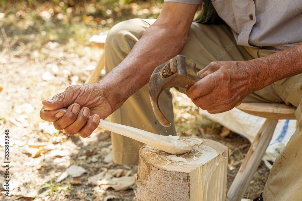 Old man handcrafting a wood sppon the traditional way of making tools ...