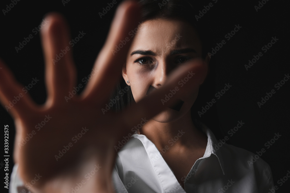Scared female victim with taped mouth on dark background. Concept of ...