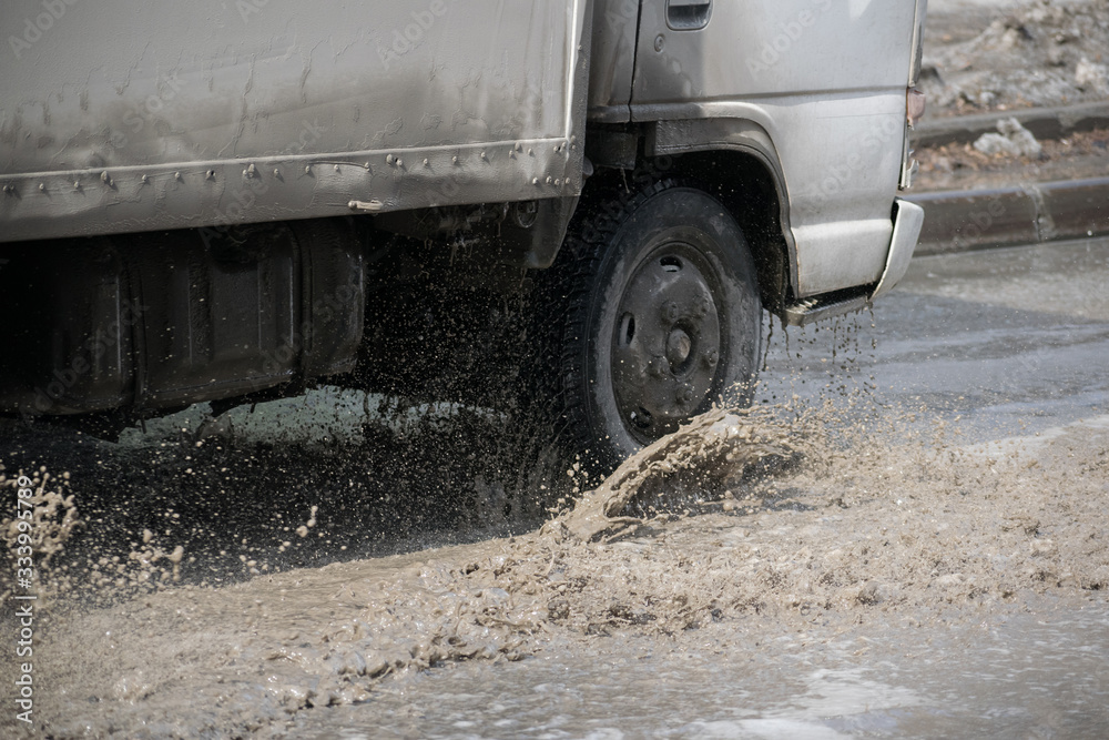 Car motion through big puddle of water splashes from the wheels on the ...