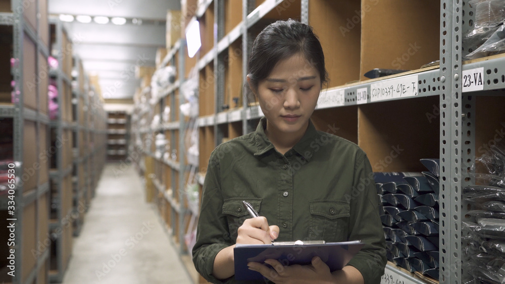 Female inventory manager checks stock and writing in clipboard ...