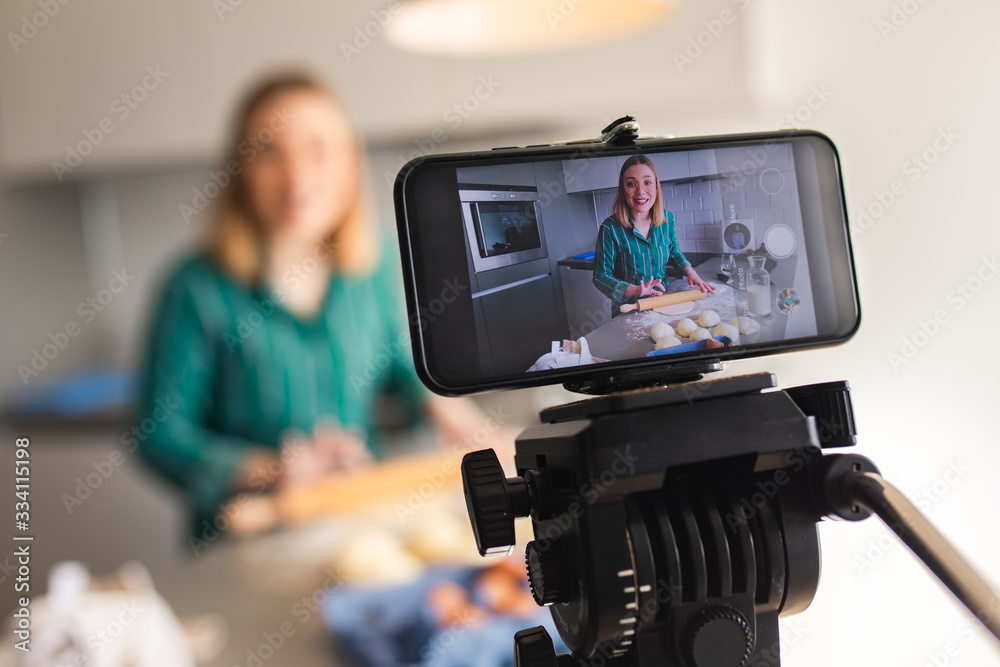 Young woman recording vlog at home in kitchen making croissants. Stock ...
