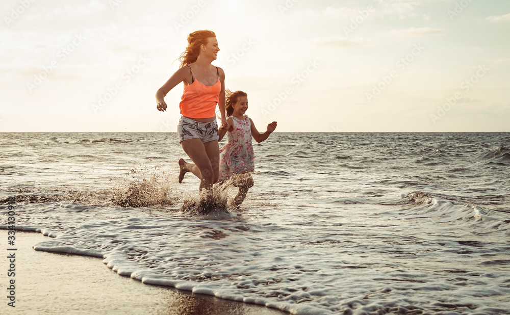 Happy loving family mother and daughter running on the beach at sunset ...