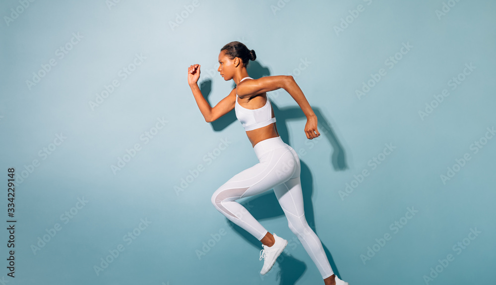 Side view of young woman running. Fitness model exercising against blue ...