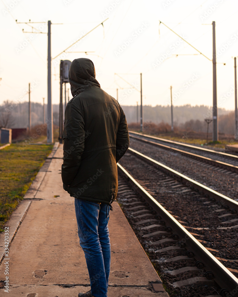 man stands at the station turned his back in the rays of a warm sun at ...