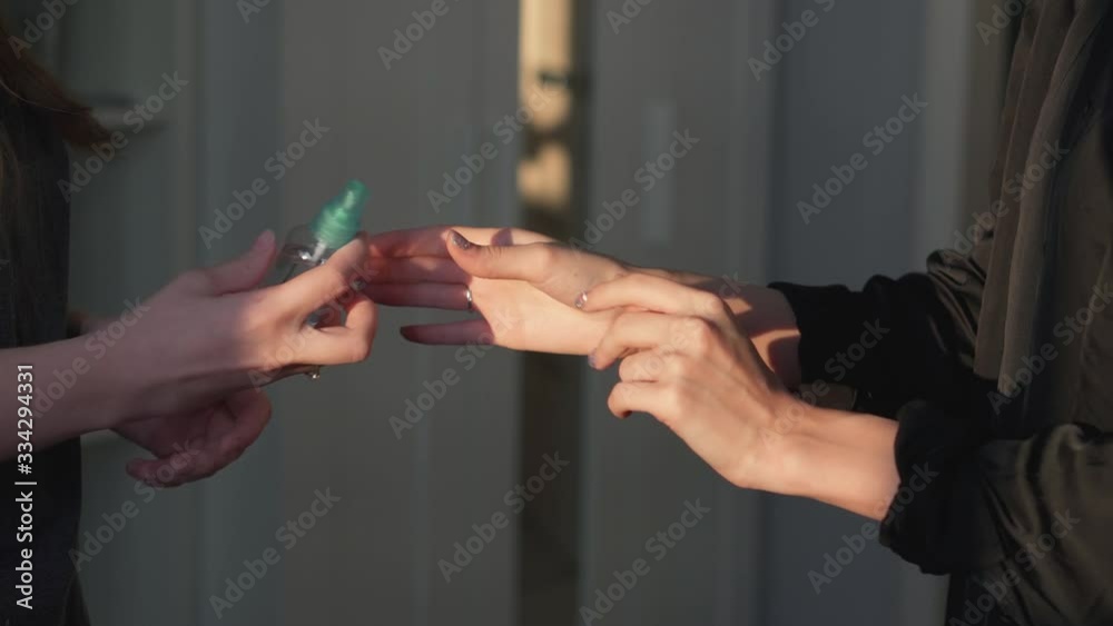 Two girls spray a hand sanitizer and rub in to clean their hands ...