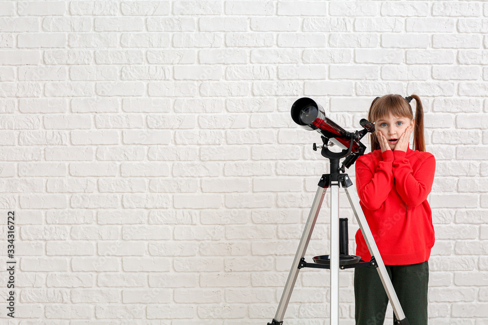 Cute surprised little girl with telescope on white brick background ...