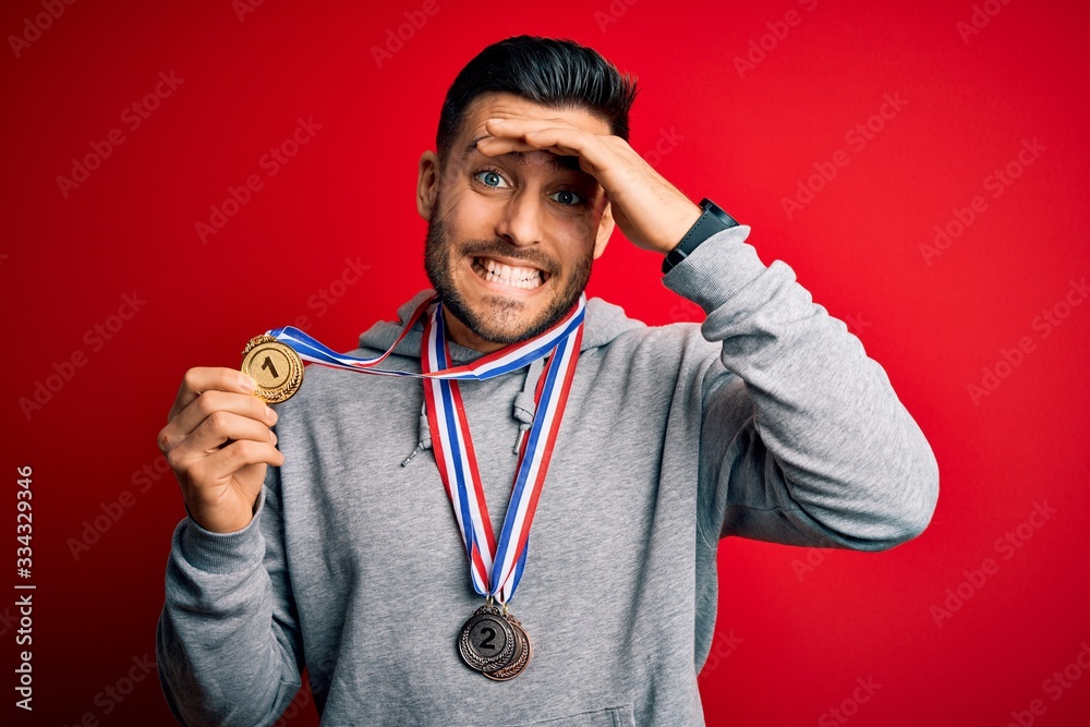 Young handsome succesful man winning medals standing over isolated red ...