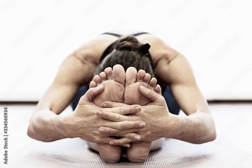 Closeup on hands of woman on seated forward bend asana grabbing feet at ...