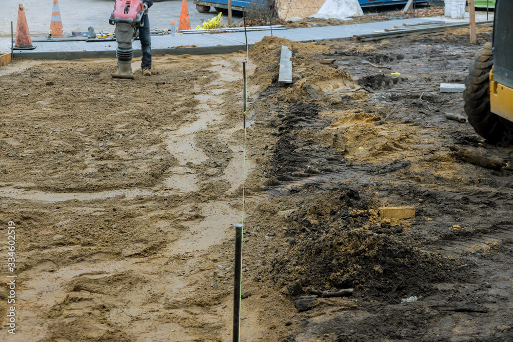 Person operating a vibratory earth rammer compacting the ground ...