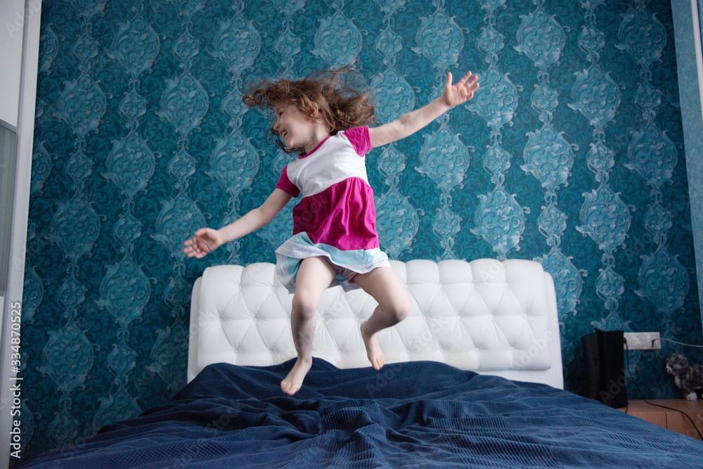 Active toddler girl dancing in bed baby jumping on white and blue bed ...