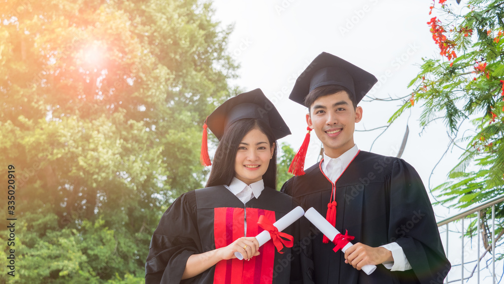 Two happy young graduates, male and female in black gown and mortar cap ...