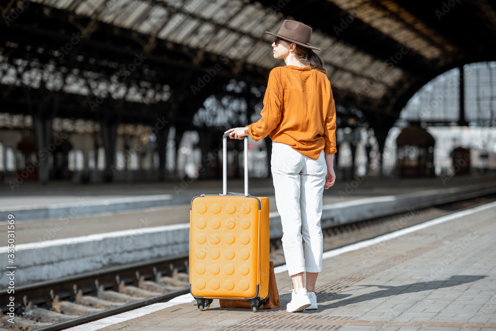 Young female traveler standing with a suitcase at the old train station ...