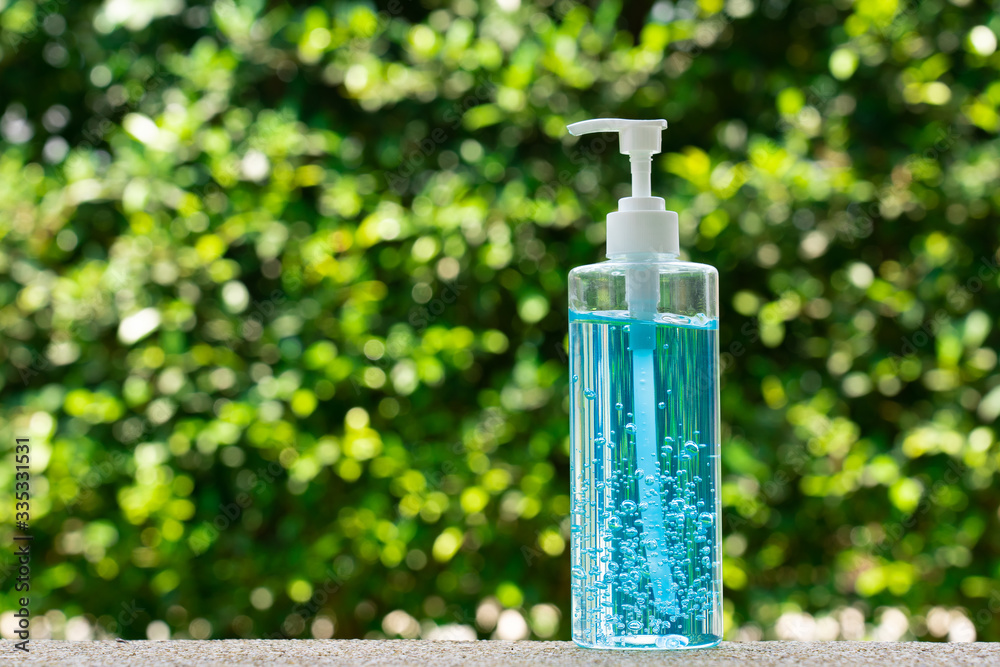 Blue hand sanitizer gel in clear pump bottle with green bokeh ...