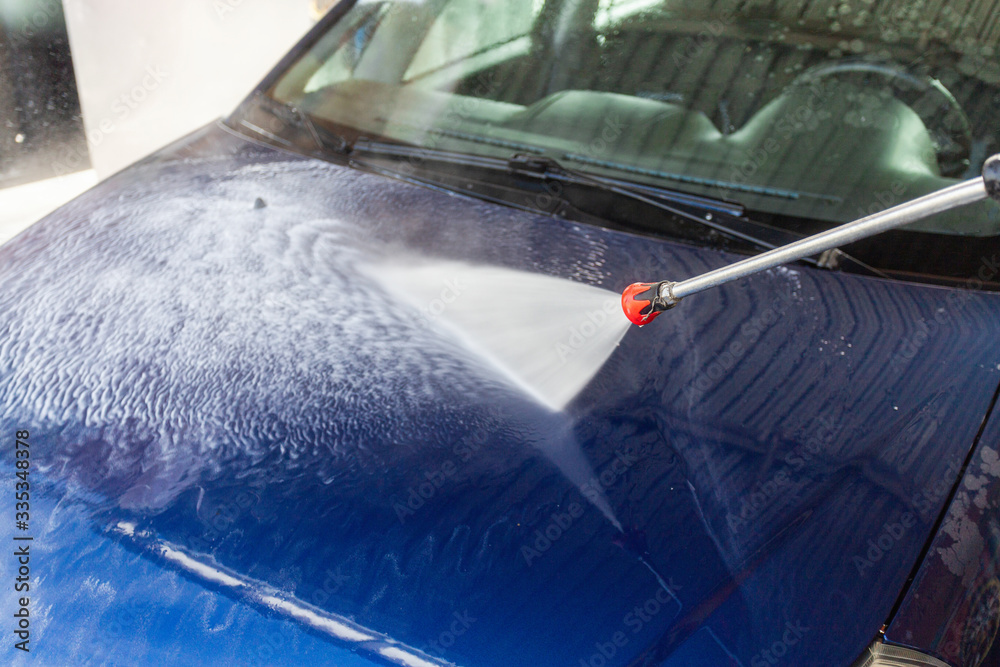 Close-up man holding a high-pressure water sprayer for car hood washing ...