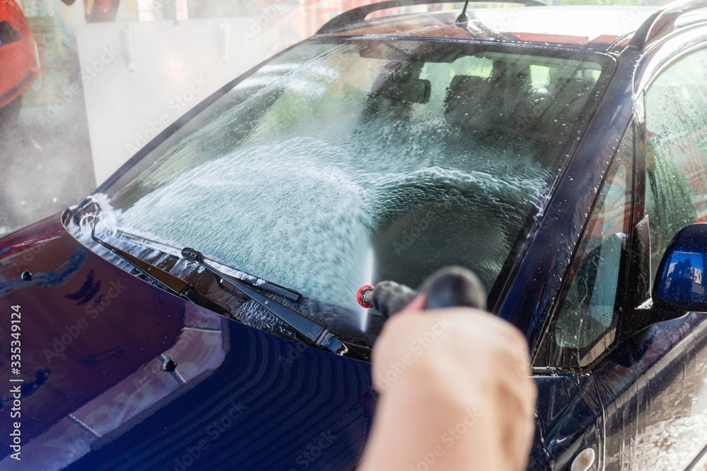 Close-up man holding a high-pressure water sprayer for car front window ...