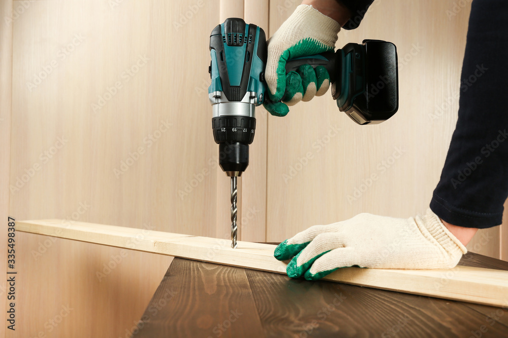 Poster worker's hand is drilling wood plank by cordless drill close up ...