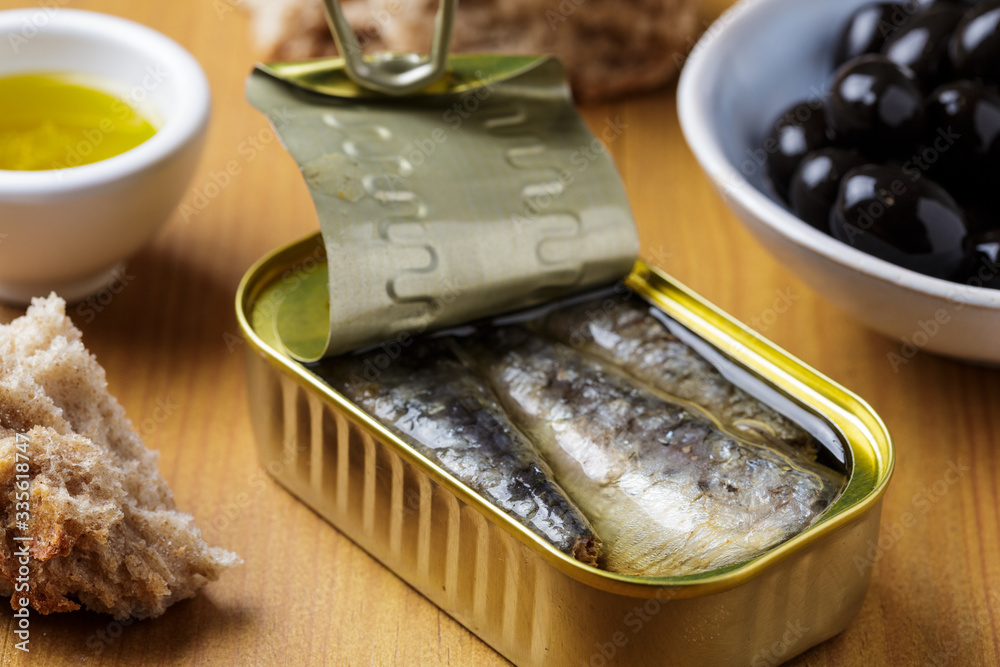 Lata de Sardinha em conserva aberta, pão azeite e azeitonas sobre mesa ...