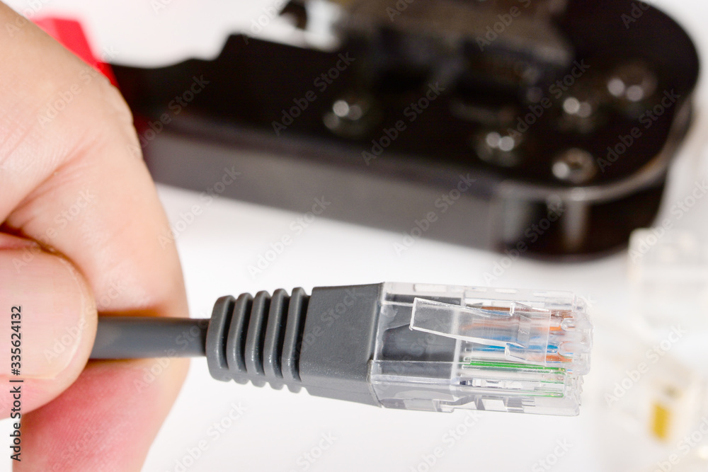 Engineer's hand holds patch cord with RJ45 connector and crimping tool ...