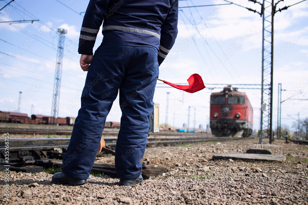 Railroader or switchman at station waving with red flag to the incoming ...