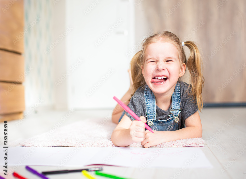 Blonde happy little girl with two ponytales drawing and writing lying ...
