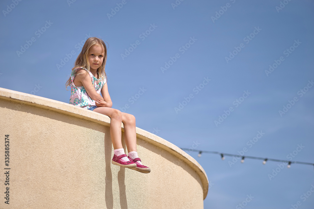 little girl sits on the edge of the wall dangling legs, stone wall her ...