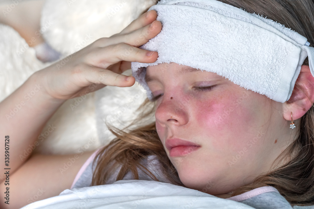 A teenage girl has flu is lying on bed with eyes closed and cold ...