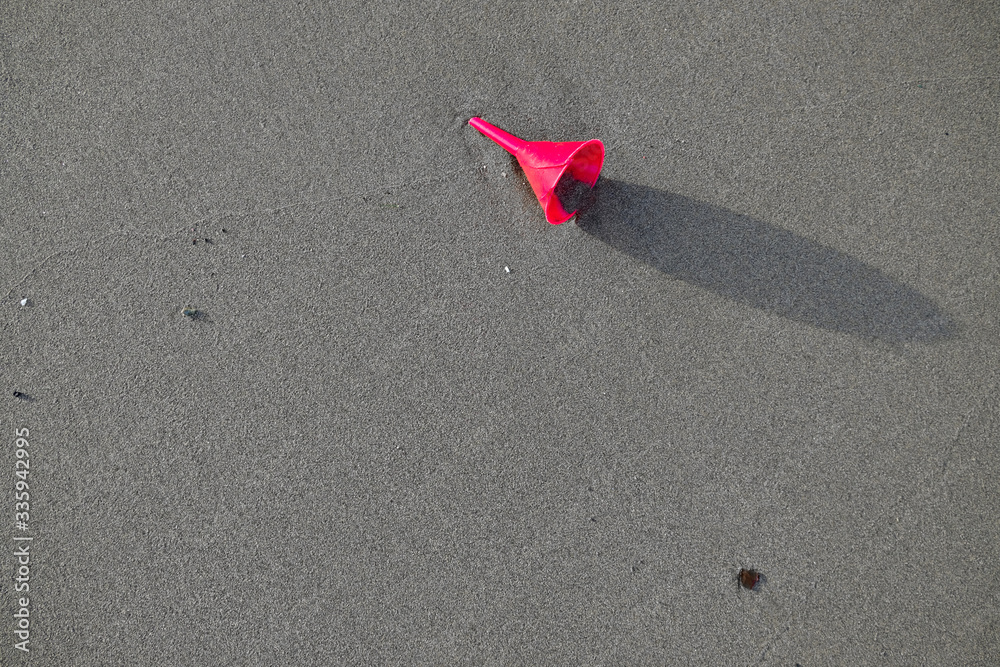 A small red funnel on the sand, role of plastic synthetic materials in ...